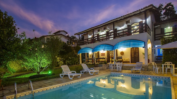 Piscina com espreguiçadeiras e guarda-sóis, rodeada por um edifício com varanda e área de estar externa.
