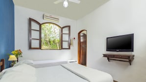 Quarto de hotel com uma cama, televisão fixada na parede e janela com vista para áreas verdes.