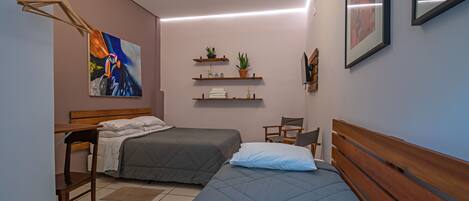 Quarto com duas camas, uma cadeira de madeira, escrivaninha e prateleiras com plantas.