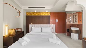 Quarto de hotel moderno com uma cama grande, cabeceira de madeira, mesa de cabeceira com abajur e banheiro com pia de mármore.