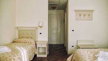 Quarto de hotel com duas camas, uma mesinha de cabeceira com abajur, uma porta com painel decorativo e um porta-toalhas fixado na parede.