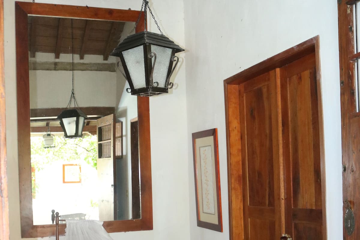 Um corredor com porta de madeira, espelho, luminária pendente e tapete de couro.