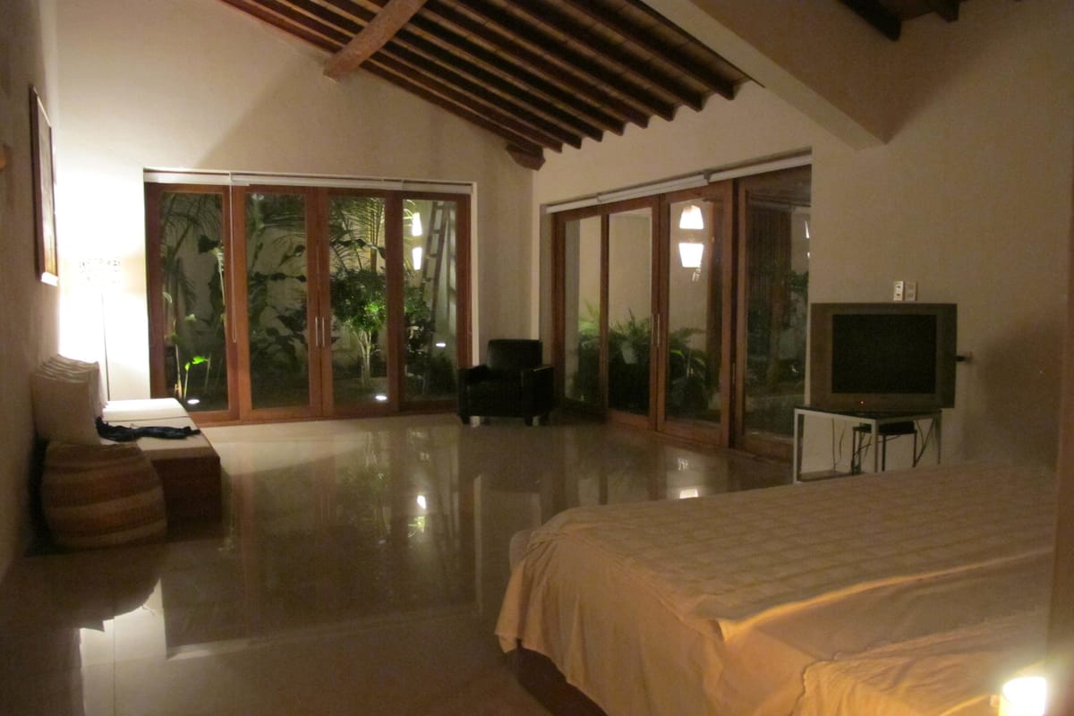 Um quarto espaçoso com uma cama grande, uma televisão e portas de correr que dão para um jardim.