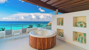 Uma banheira de hidromassagem circular com detalhes em madeira, cadeiras brancas e objetos decorativos numa varanda com vista para o mar.