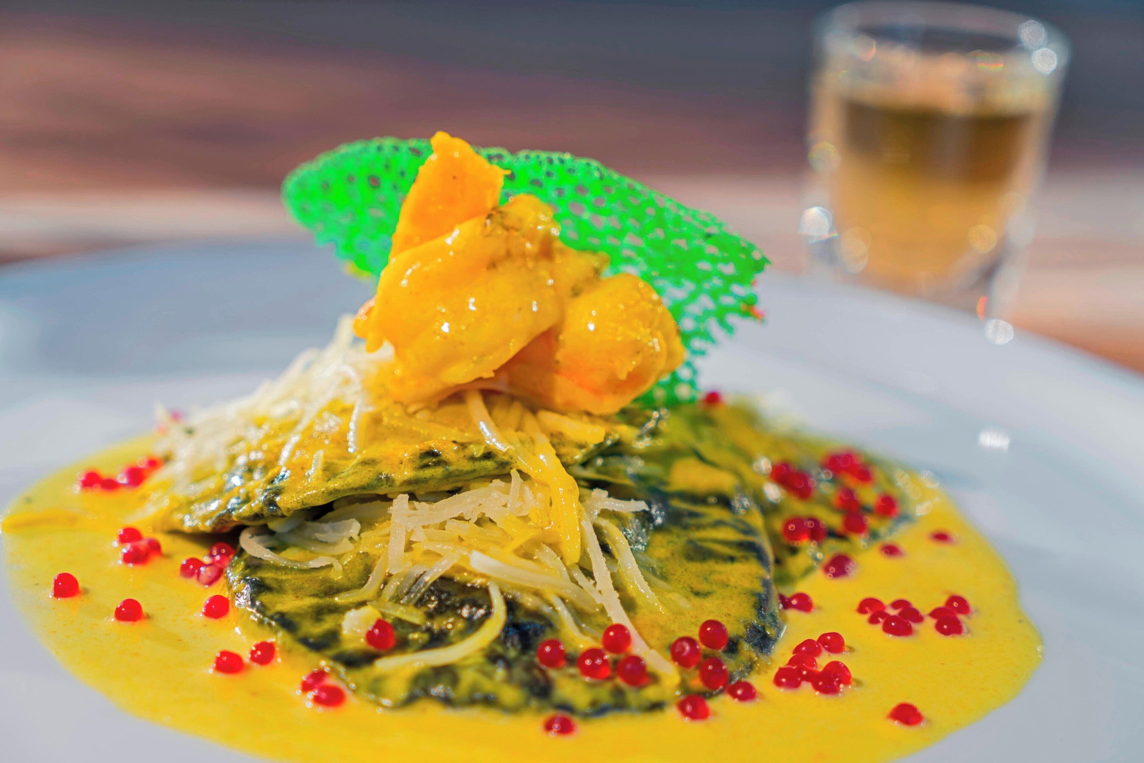 Um prato com guarnição verde, um copo de bebida e amoras vermelhas.
