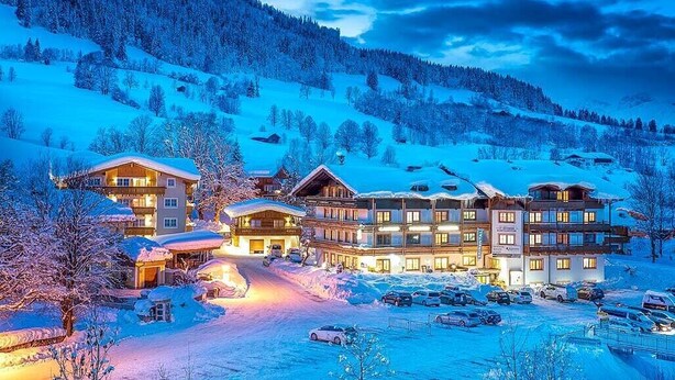 Um hotel grande, com vários andares, com um teleférico visível ao fundo, rodeado por colinas cobertas de neve.