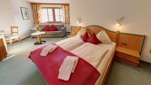 Quarto de hotel com uma cama grande, um sofá, uma mesinha com flores e uma janela com cortinas.