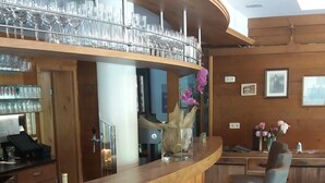 Uma área de bar com balcão de madeira, banquetas e um vaso com flores.