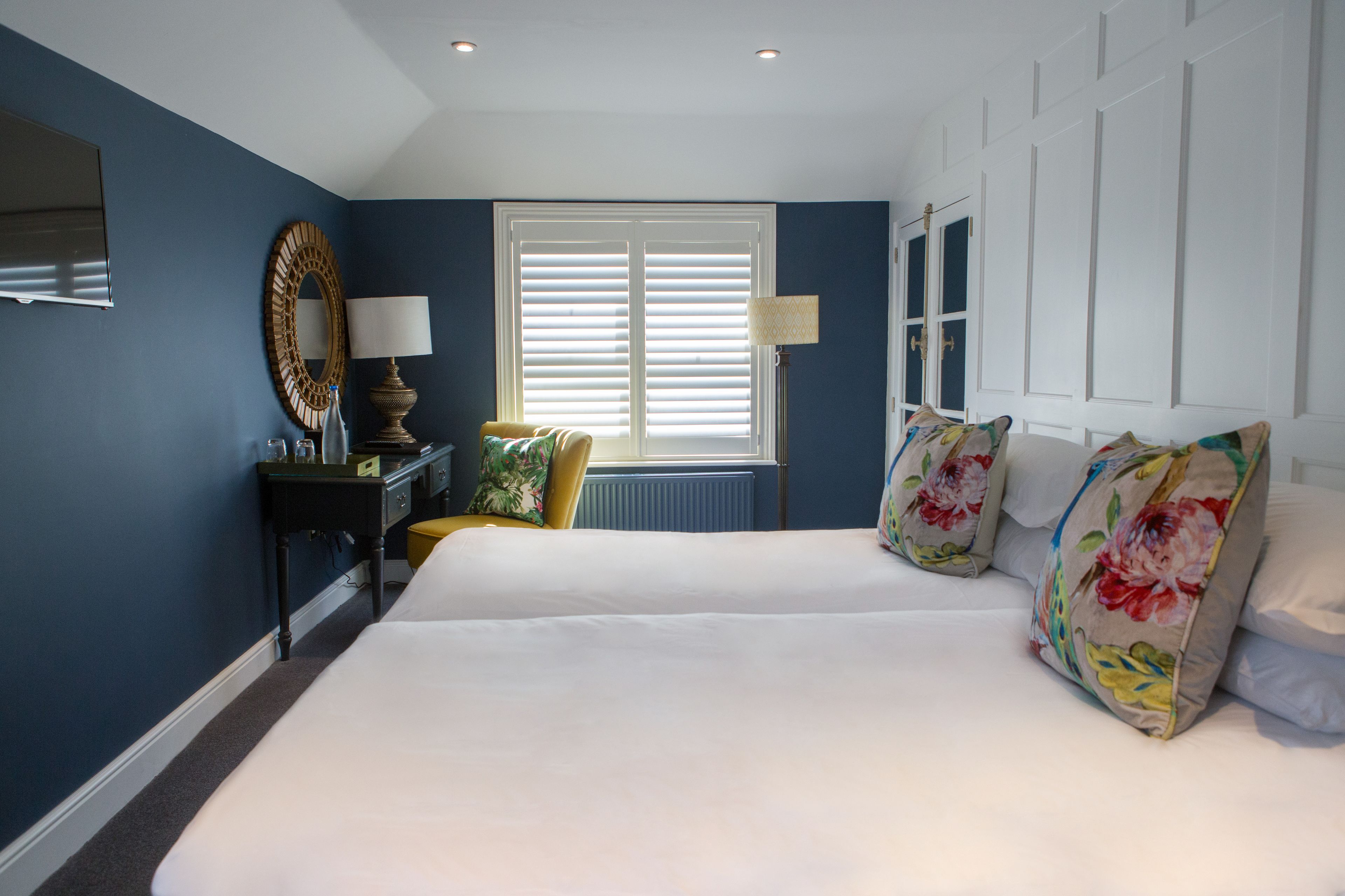 Quarto com cama grande, escrivaninha com abajur, cadeira e janela com persianas.