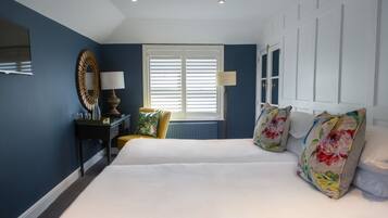 Quarto com cama grande, escrivaninha com abajur, cadeira e janela com persianas.