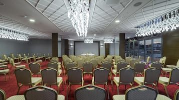 Uma sala de conferências com fileiras de cadeiras, um palco e uma grande janela com vista.