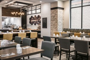Um restaurante moderno com paredes de madeira e pedra, um espaço de bar e mesas e cadeiras bem organizadas.