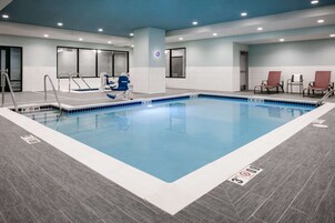 Piscina interna com pistas demarcadas, cadeira do salva-vidas e área de vestiários.