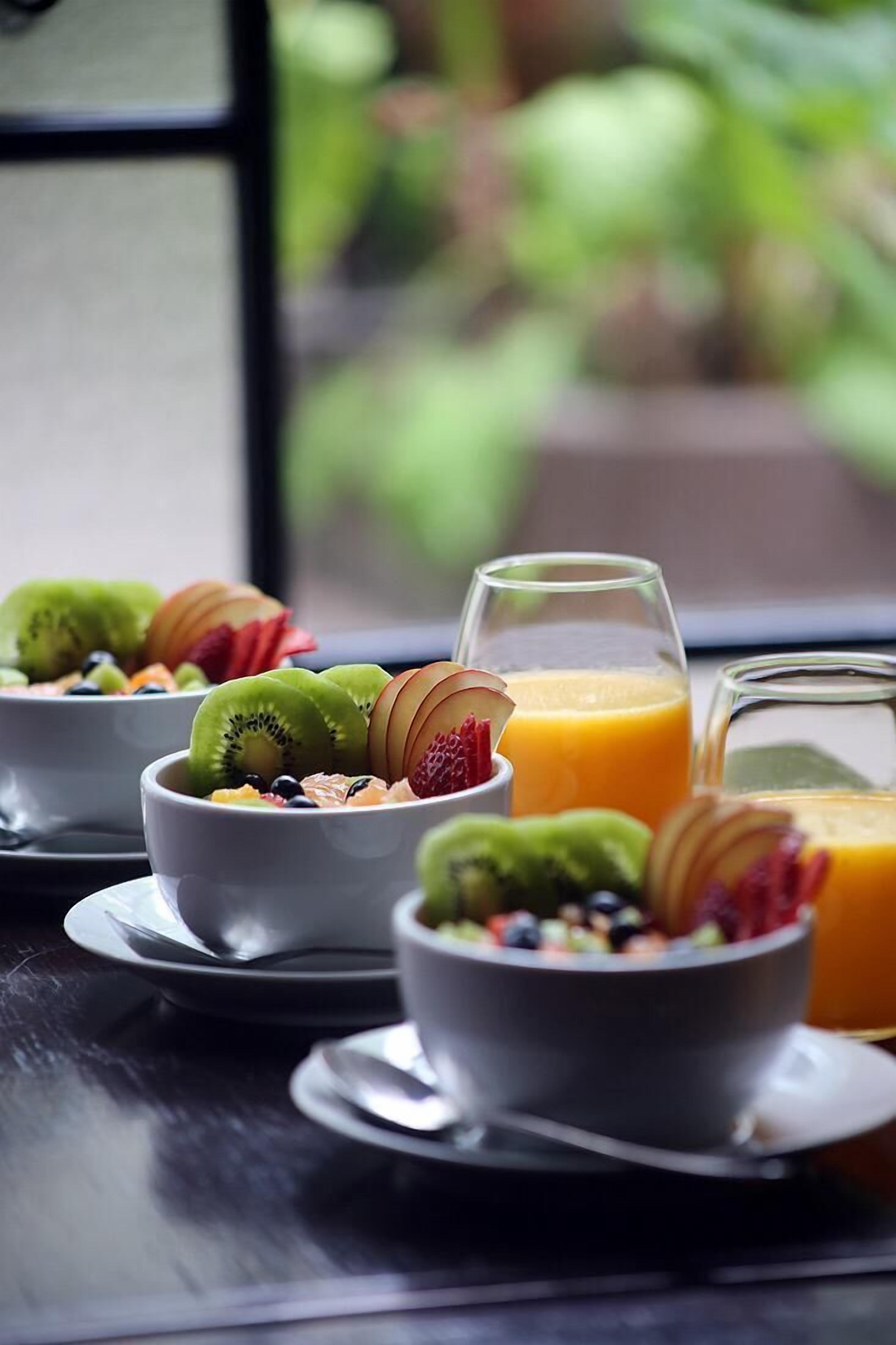 Disposição para o café da manhã com tigelas de frutas e um copo de suco de laranja sobre uma mesa.