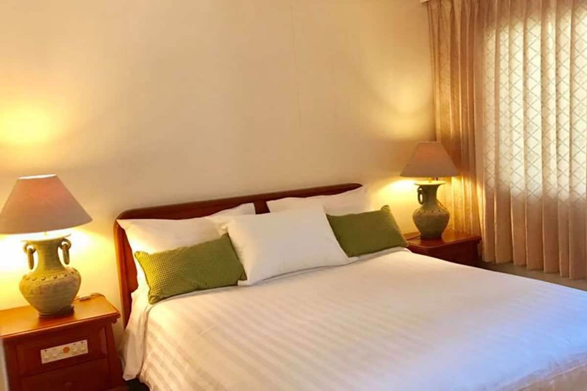 Quarto de hotel com uma cama grande, duas luminárias laterais e uma janela com cortinas.