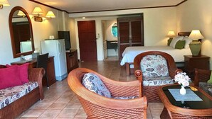 Quarto de hotel com móveis de vime, uma cama, uma escrivaninha e uma televisão.