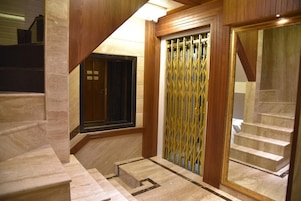Uma escadaria com degraus de mármore e lambris de madeira, conduzindo a um quarto com um espelho grande e um portão decorativo.