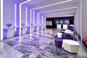 Um hall de hotel moderno, com um balcão de recepção extenso, estações de trabalho individuais e uma área de estar.