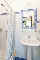 Casa de banho com chuveiro, pia e espelho.