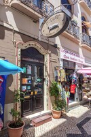 Fachada de loja com uma placa que diz "Bicuar" e "Loja Goa Indian Goa Indian Shop", exibindo diversos artigos de vestuário do lado de fora.