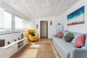 Uma sala de estar moderna com sofá, poltrona amarela, mesa consola branca e uma janela grande.