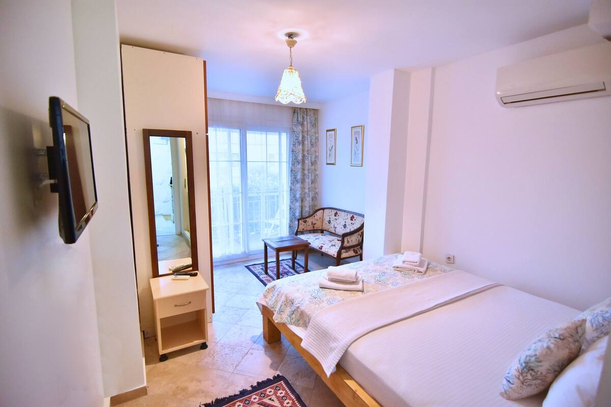 Quarto com cama, mesa de cabeceira, espelho, cadeira e janela.