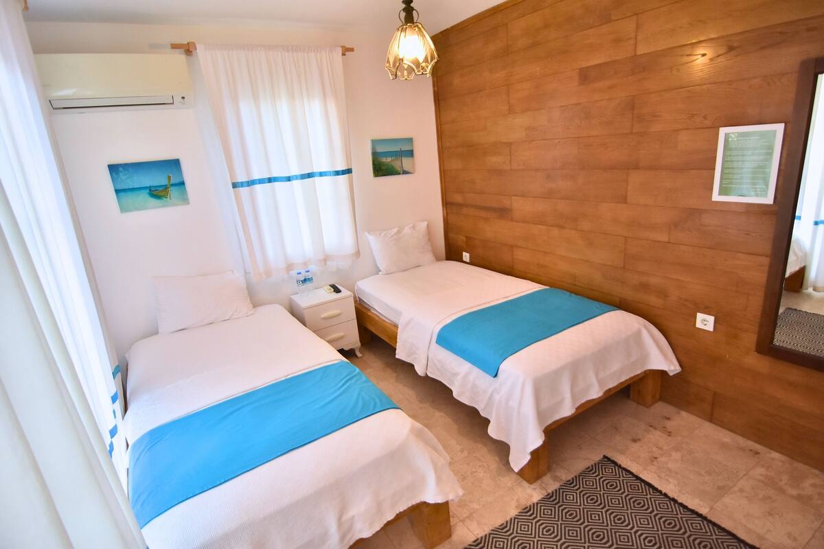 Quarto com duas camas, uma mesa de cabeceira, ar-condicionado fixado na parede e painel de parede de madeira.