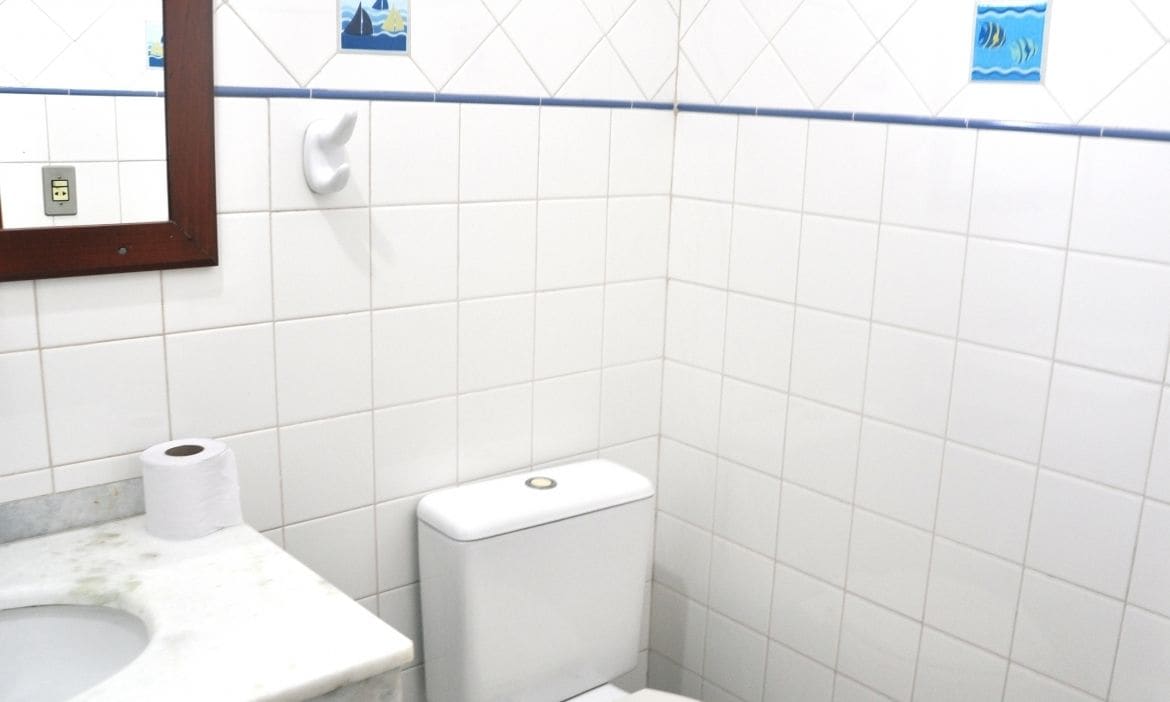 Casa de banho pequena com azulejos brancos, sanita, lavatório e espelho.