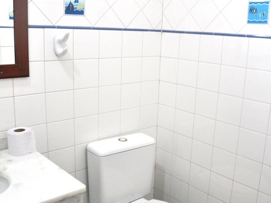 Casa de banho pequena com azulejos brancos, sanita, lavatório e espelho.