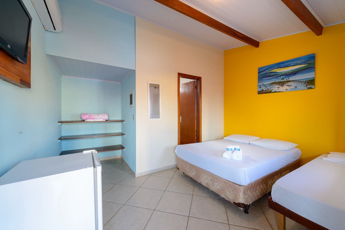 Quarto de hotel com cama, uma pequena mesa de escritório, uma cadeira, janela e um quadro na parede.