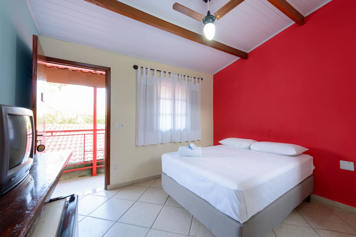 Quarto com cama, televisão e janela com cortinas.