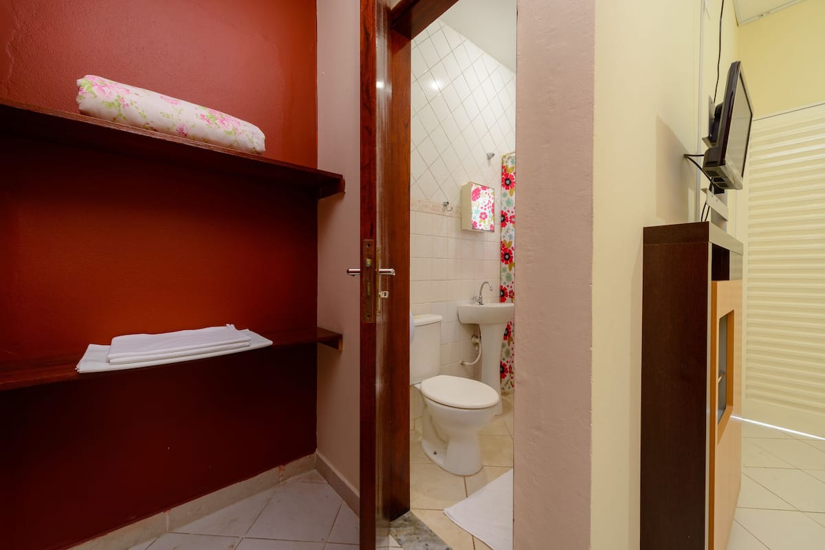 Casa de banho com sanita, lavatório e prateleiras com toalhas.