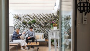 Uma área de estar moderna ao ar livre, com cerca de metal, plantas em vasos e uma mesa de vidro.
