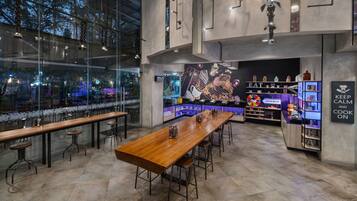Uma área de bar moderna com um balcão de madeira comprido, vários bancos e um mural na parede de fundo.