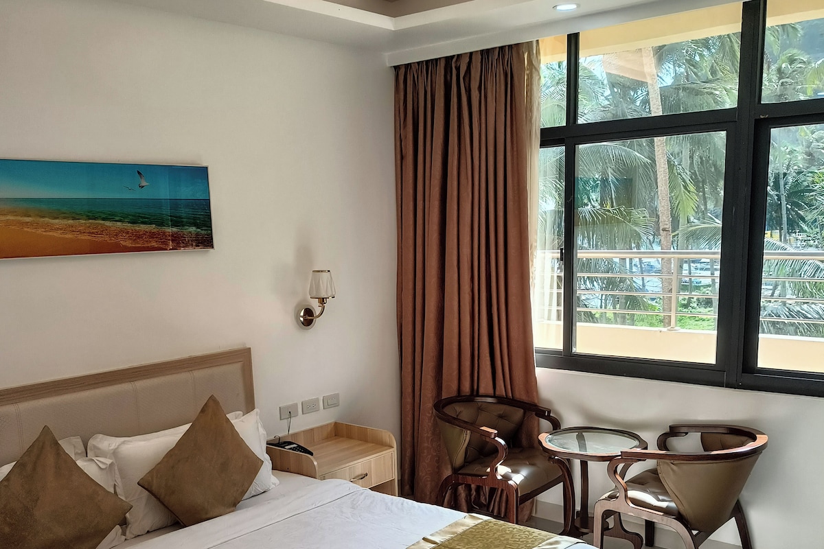 Quarto de hotel com cama, escrivaninha, cadeira, janela com cortinas e um quadro na parede.