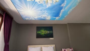 Quarto de hotel com cama, mesa de cabeceira, travesseiro, um mural no teto e uma pintura na parede.