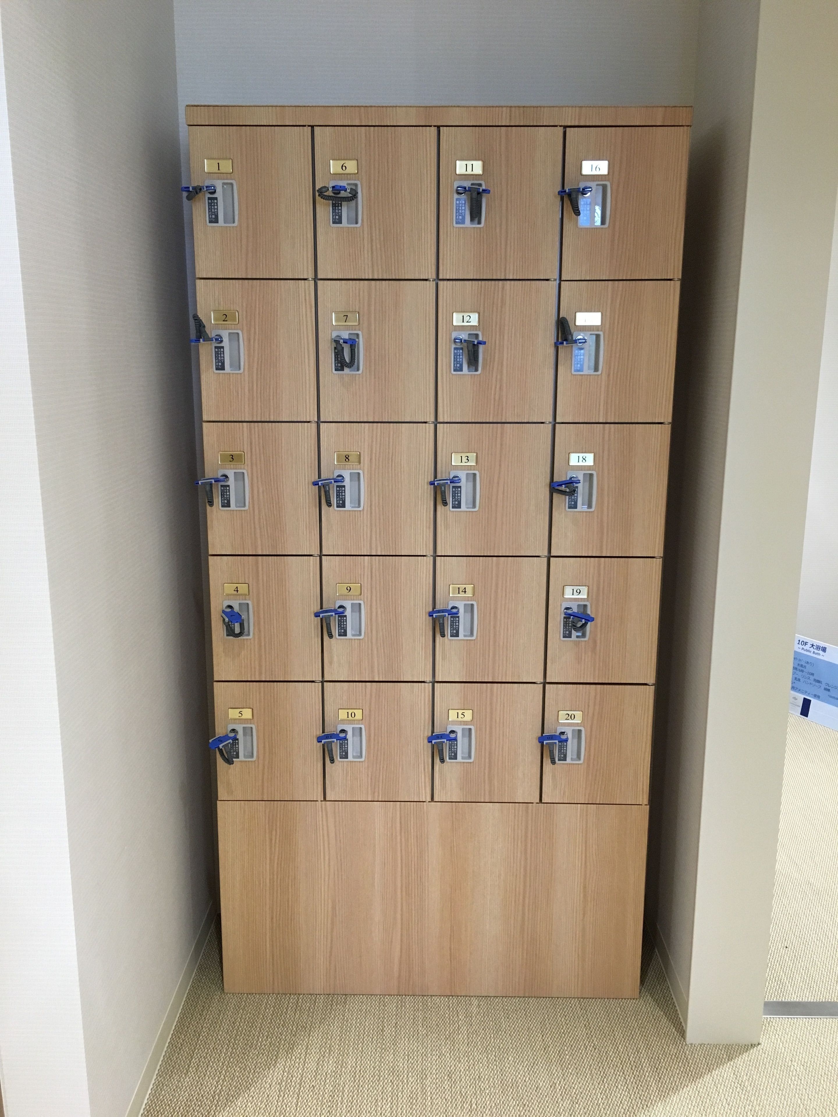 Fileira de armários de madeira com etiquetas numeradas, cada um equipado com um telefone e uma fechadura.