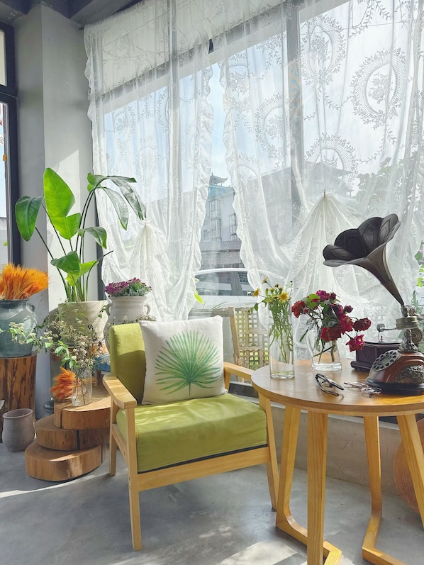 Quarto com sofá verde, mesa de madeira e diversos vasos de plantas.