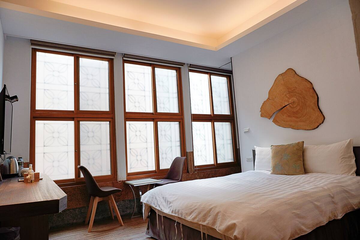 Quarto com uma cama grande, uma escrivaninha com cadeira e uma janela com persianas.