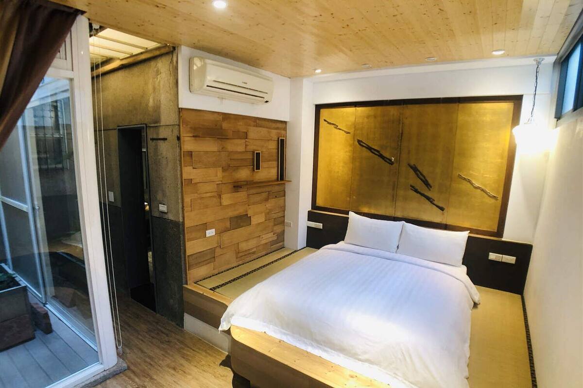 Quarto de hotel moderno com cabeceira de madeira, uma cama grande e um aparelho de ar condicionado fixado na parede.