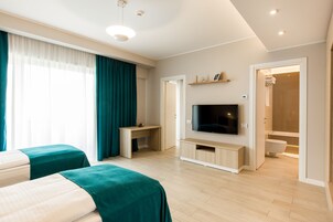 Quarto de hotel moderno com duas camas, televisão, escrivaninha e zona de chuveiro.