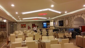Um restaurante com várias mesas e cadeiras, uma área de bar e uma tela de televisão.
