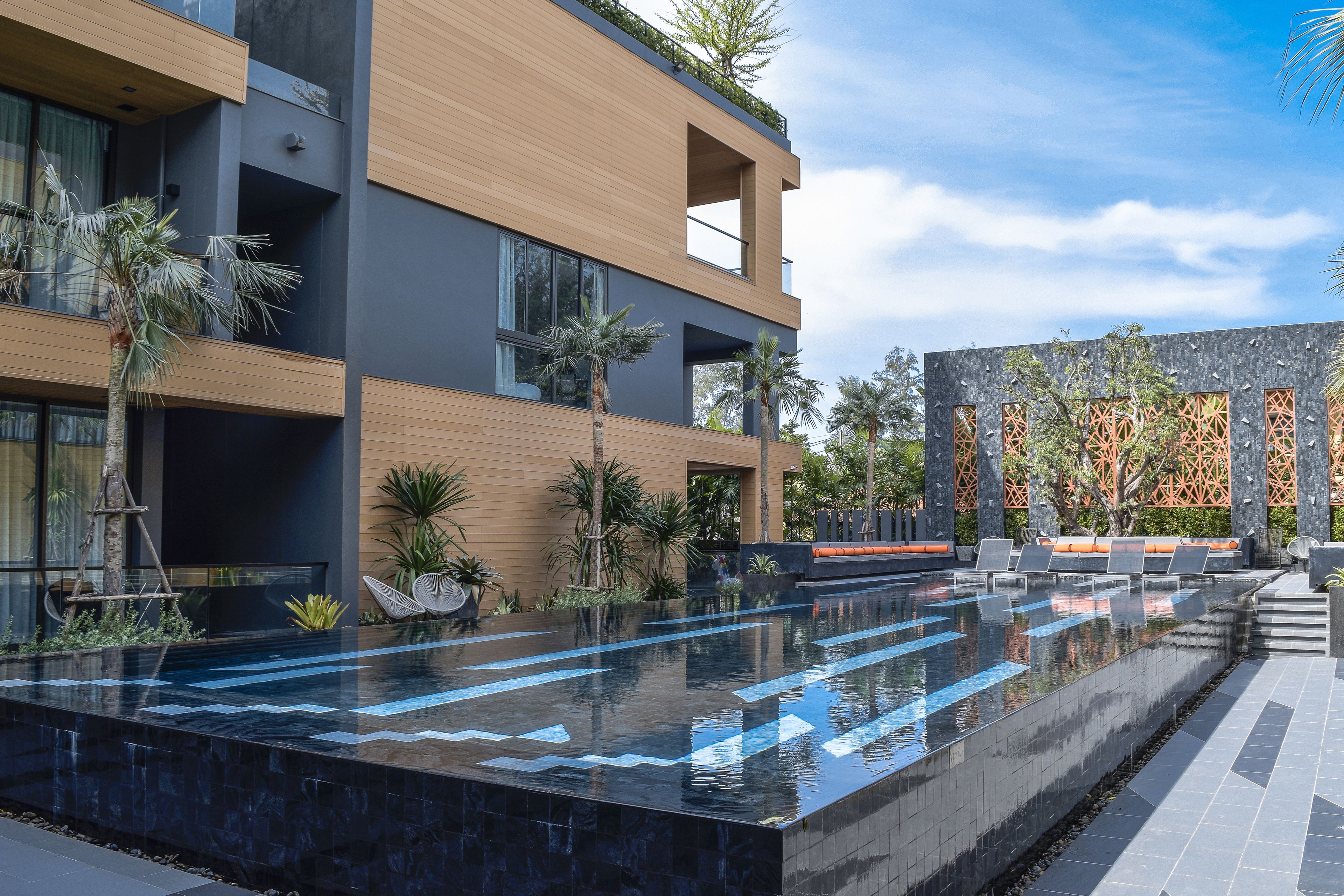 Um edifício moderno com piscina, área de estar externa e uma combinação de painéis de madeira e cores escuras.