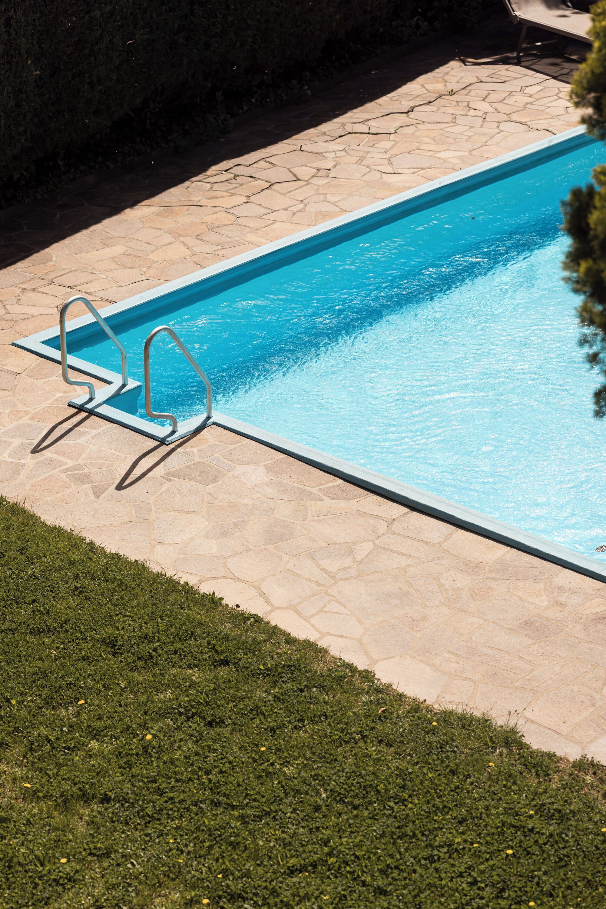 Piscina retangular com borda de pedra e escada de metal.