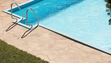 Piscina retangular com borda de pedra e escada de metal.