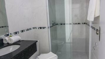 Um banheiro moderno com chuveiro em box de vidro, vaso sanitário branco e bancada de mármore preto.