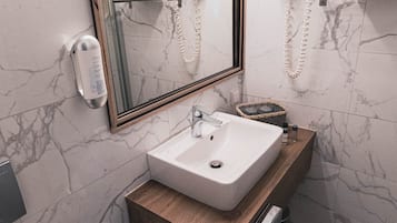 Casa de banho com parede revestida a mármore, um espelho grande, uma pia, um porta-toalhas, um secador de cabelo e um suporte de papel higiénico.