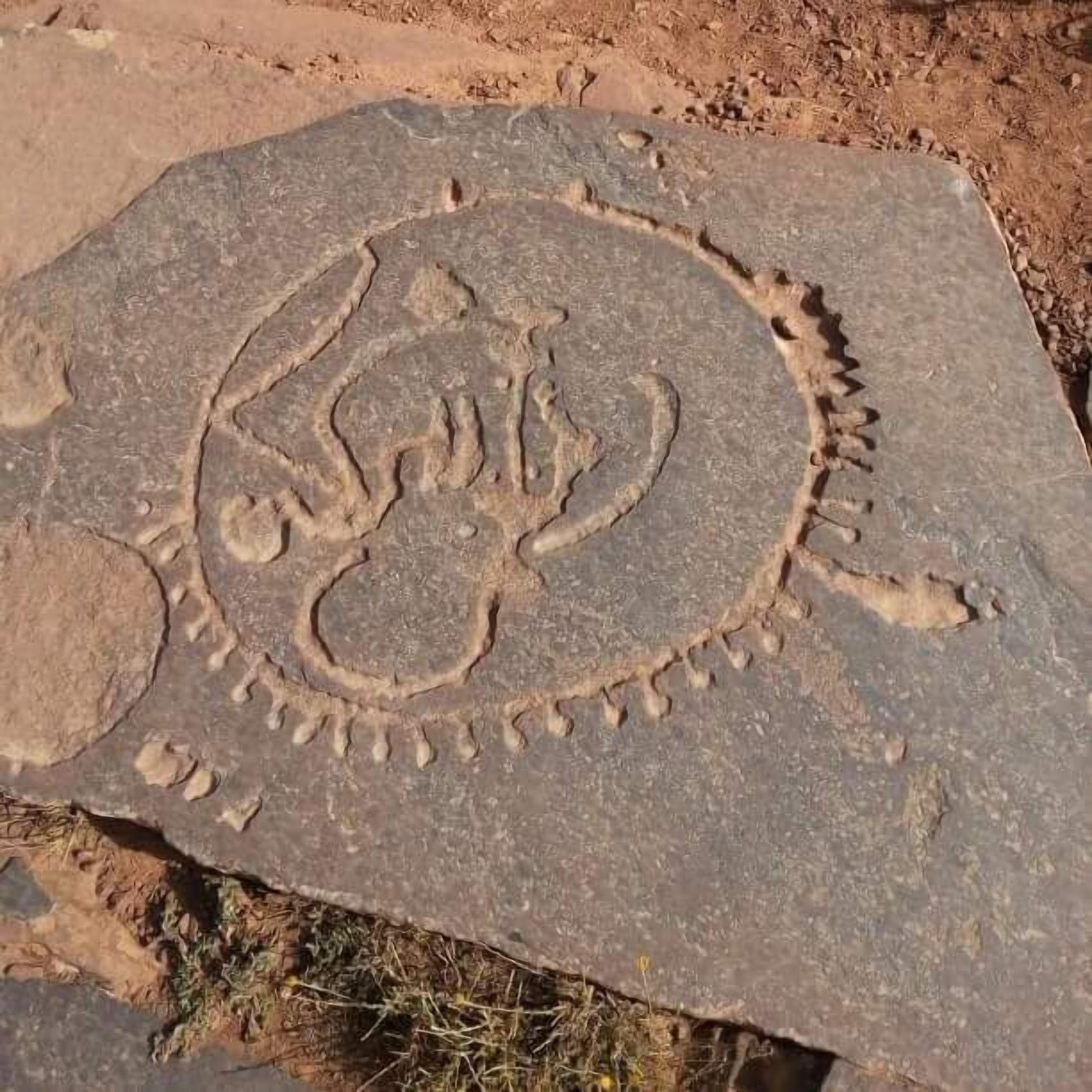 Uma pedra com uma figura esculpida, possivelmente uma divindade, rodeada por um padrão circular.