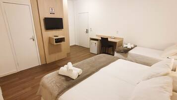 Quarto de hotel com uma cama grande, uma escrivaninha com cadeira, uma televisão na parede e um pequeno frigorífico.