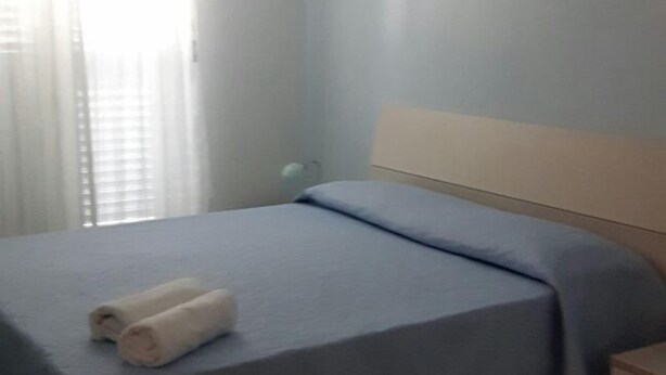 Quarto com cama, mesa de cabeceira, abajur e janela com persianas.
